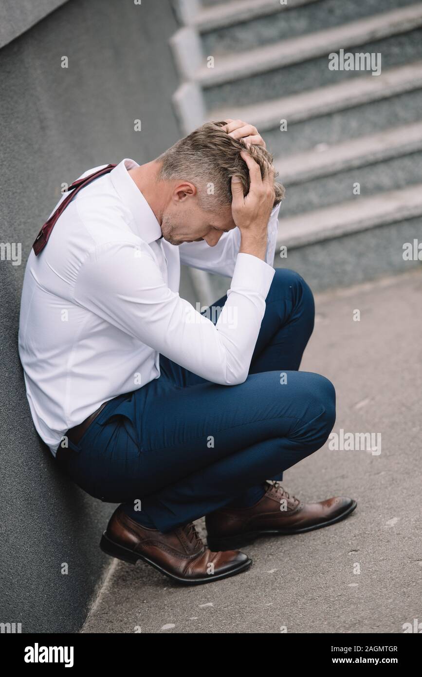 upset businessman sitting and touching head near stairs Stock Photo - Alamy