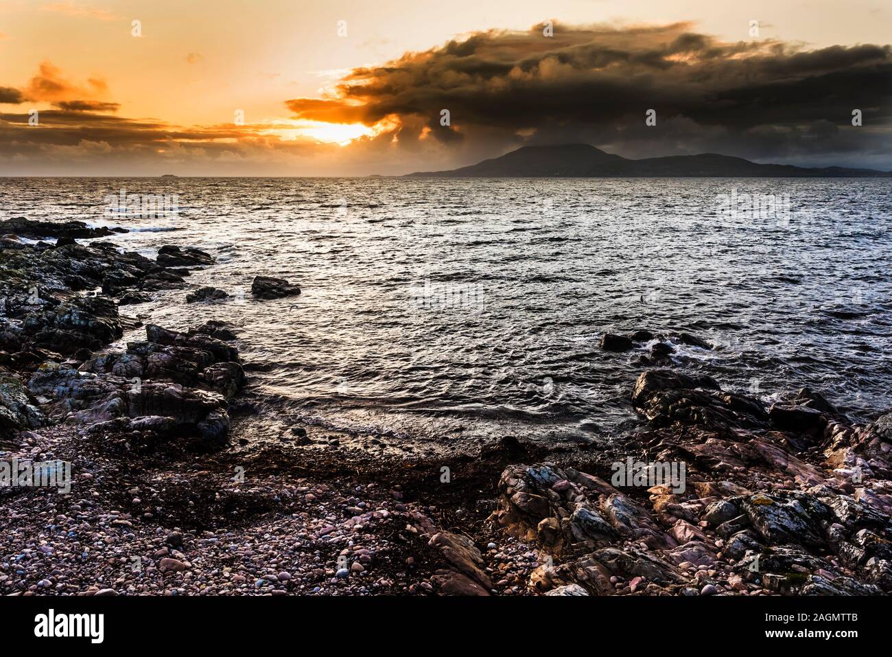 View across a turbulent sea at sunset towards Clare Island from Roonagh ...