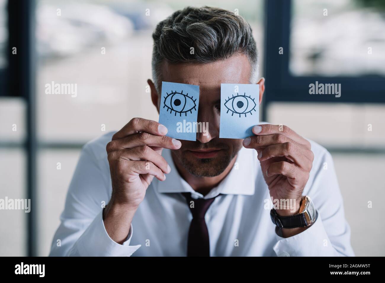 businessman in suit holding sticky notes with drawn eyes near face ...