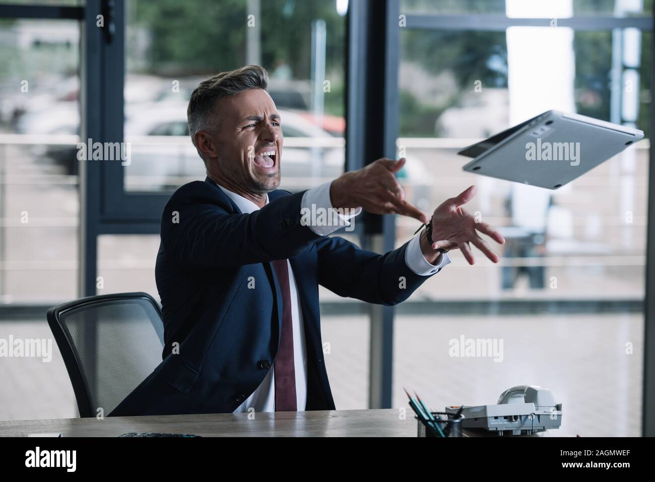 angry businessman throwing in air laptop in office Stock Photo - Alamy