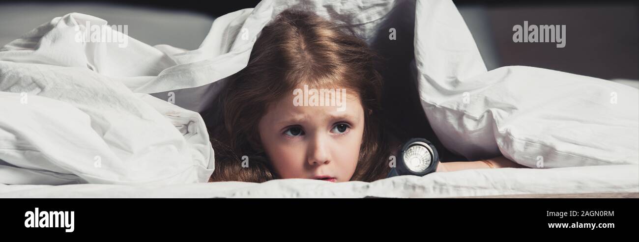 scared child hiding under blanket with flashlight isolated on black ...