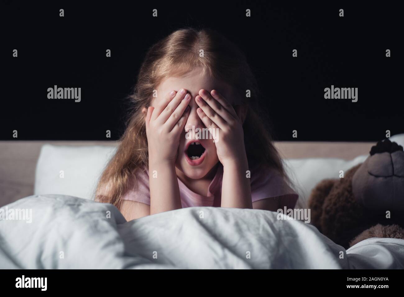 frightened kid screaming and covering eyes with hands while sitting on ...