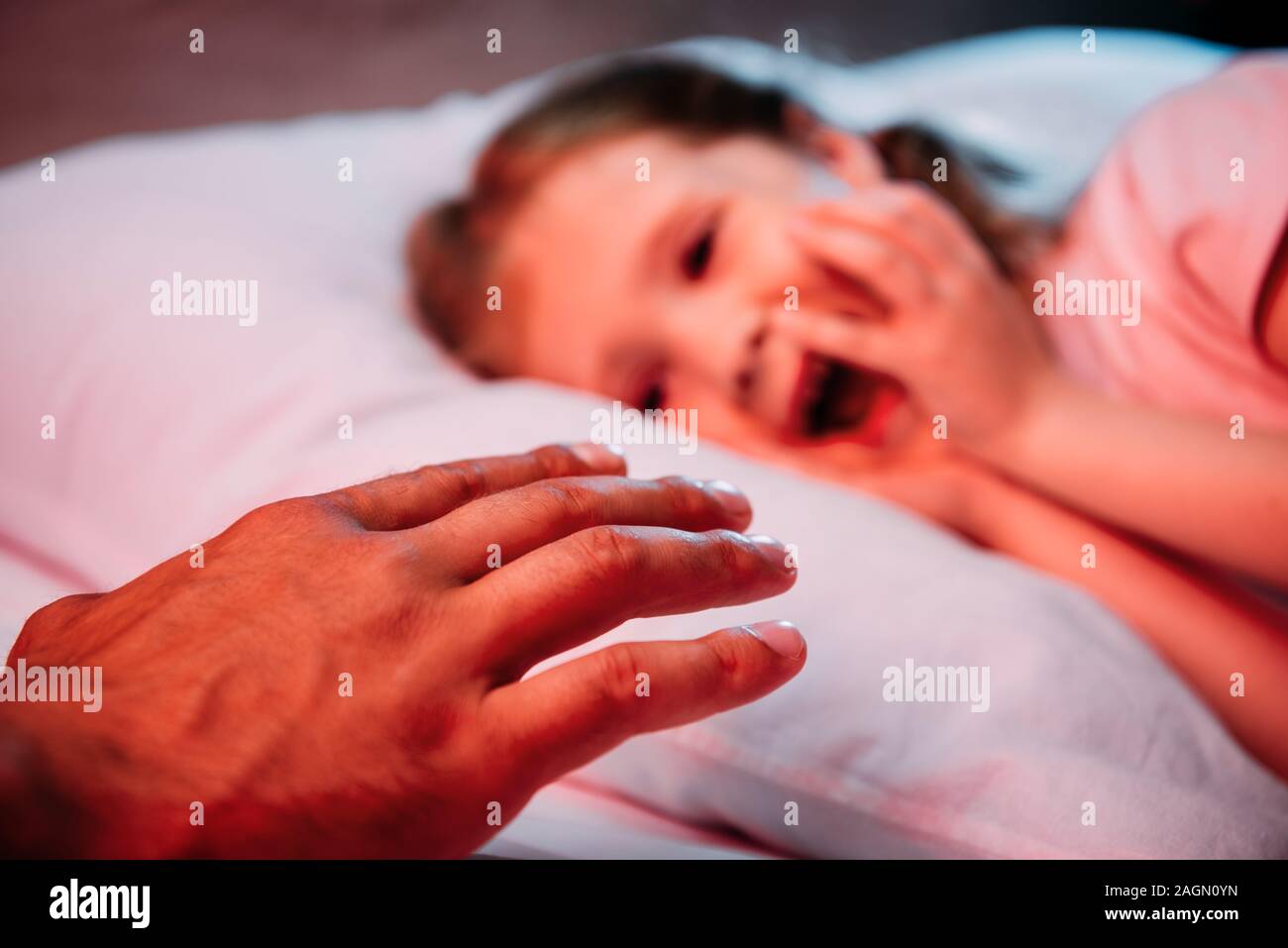 selective focus of male hand near scared, screaming child lying in bed ...