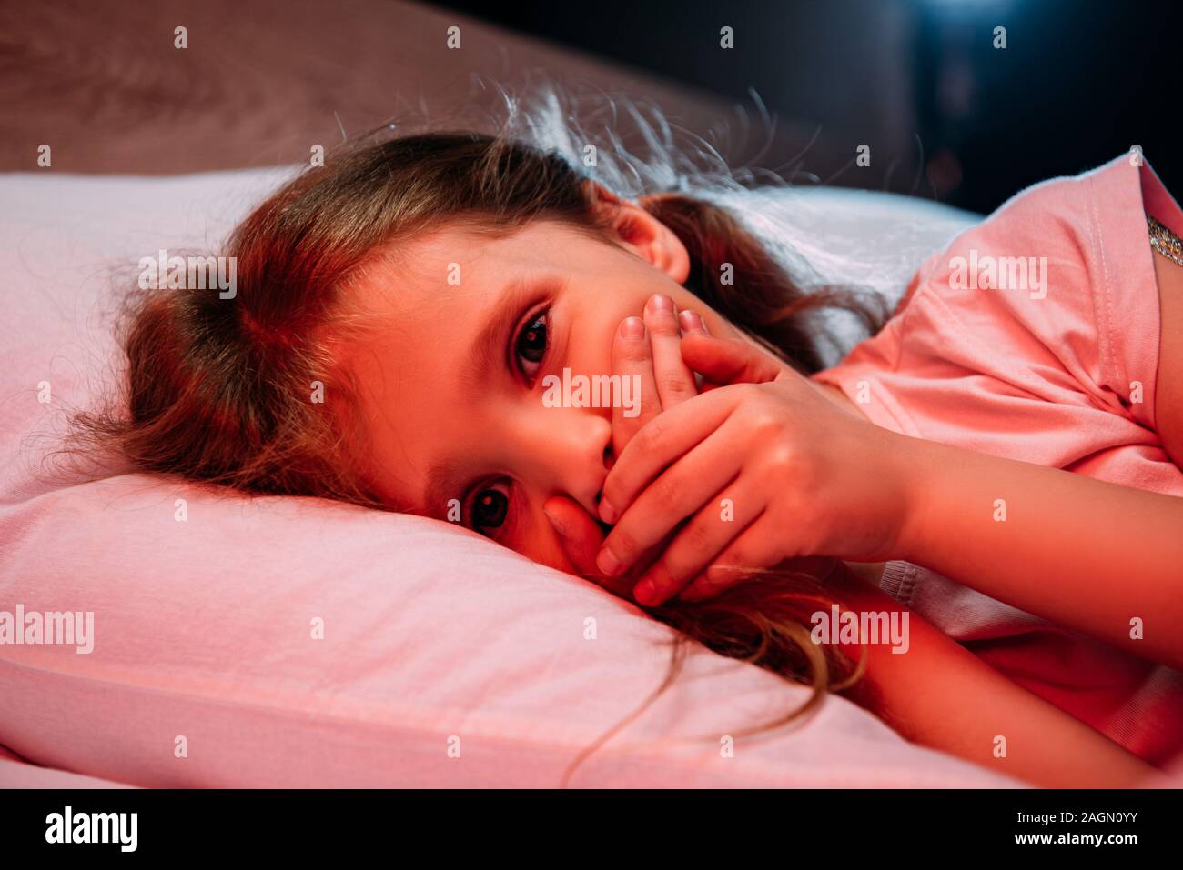 scared child looking at camera while lying in bed and showing hush sign ...