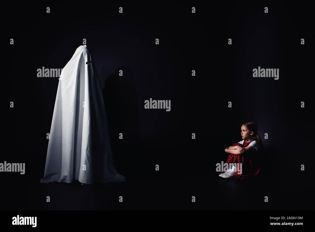 scared child sitting on floor and looking at terrible white ghost on ...