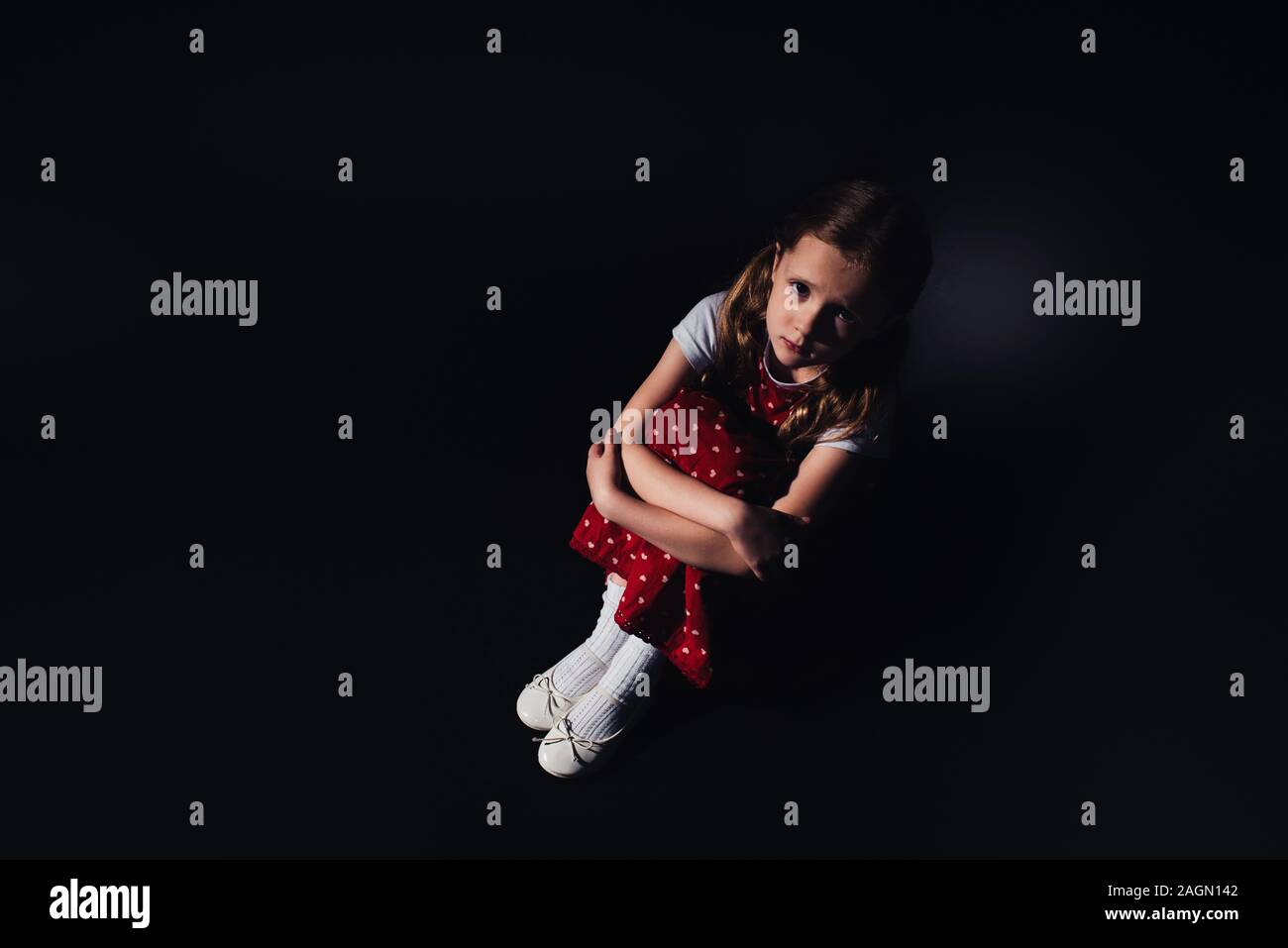 sad, scared child sitting on floor and looking at camera on black ...