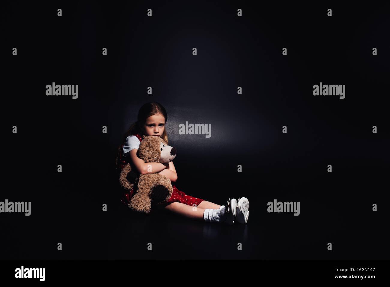 lonely, scared kid sitting on floor and hugging teddy bear on black ...