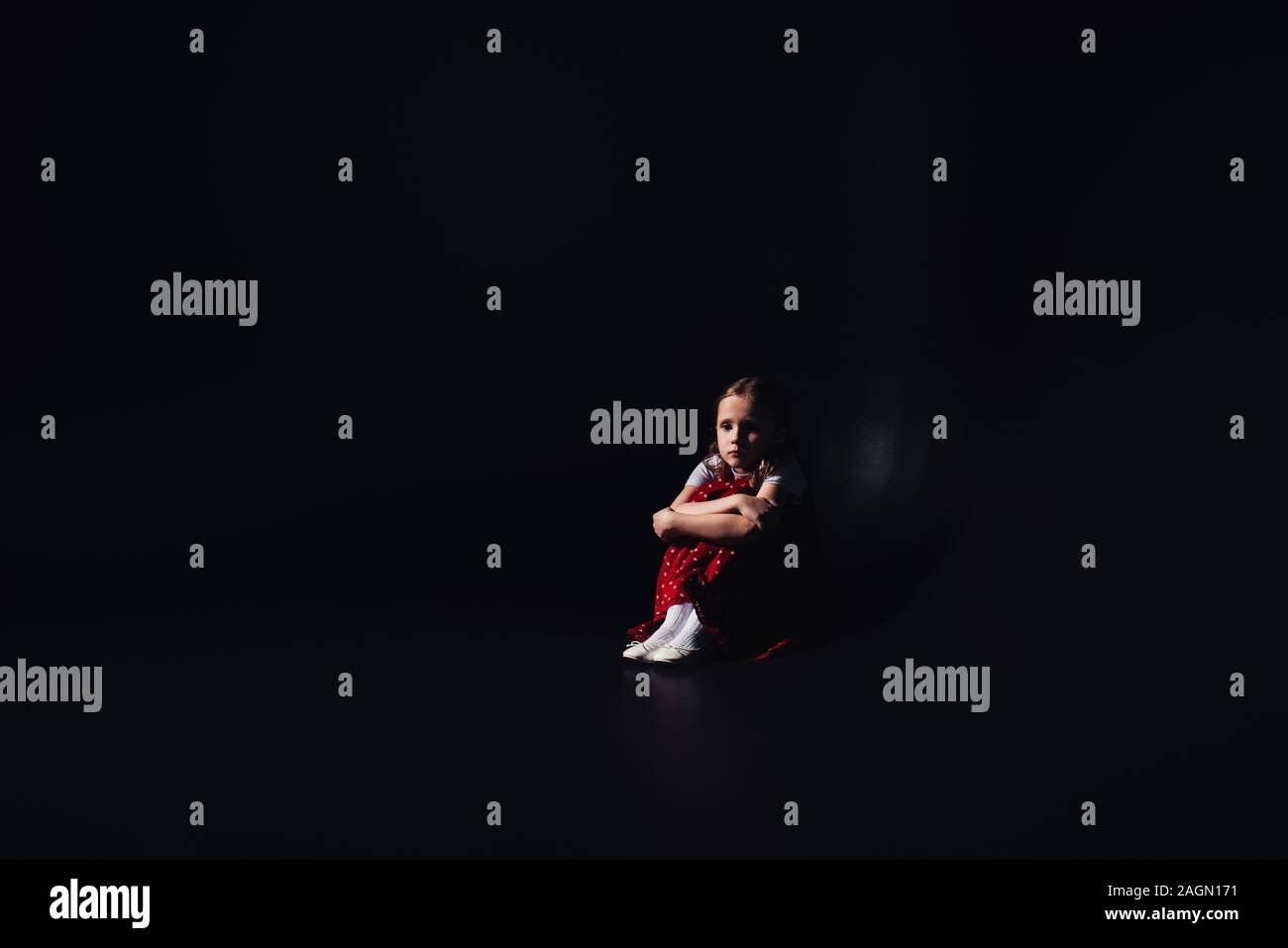 scared, lonely child sitting on floor on black background with copy ...