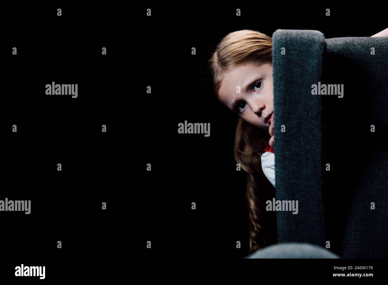 scared child looking at camera while hiding behind armchair isolated on ...