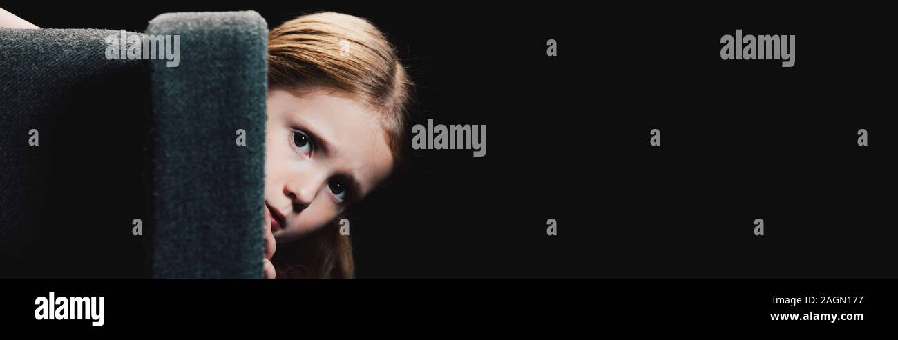 panoramic shot of scared child looking at camera while hiding behind ...