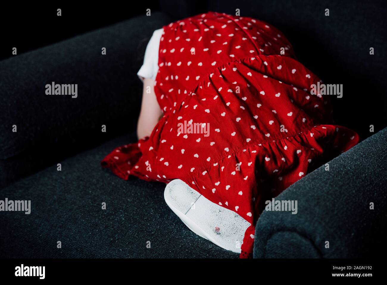 depressed, scared child hiding in armchair isolated on black Stock ...