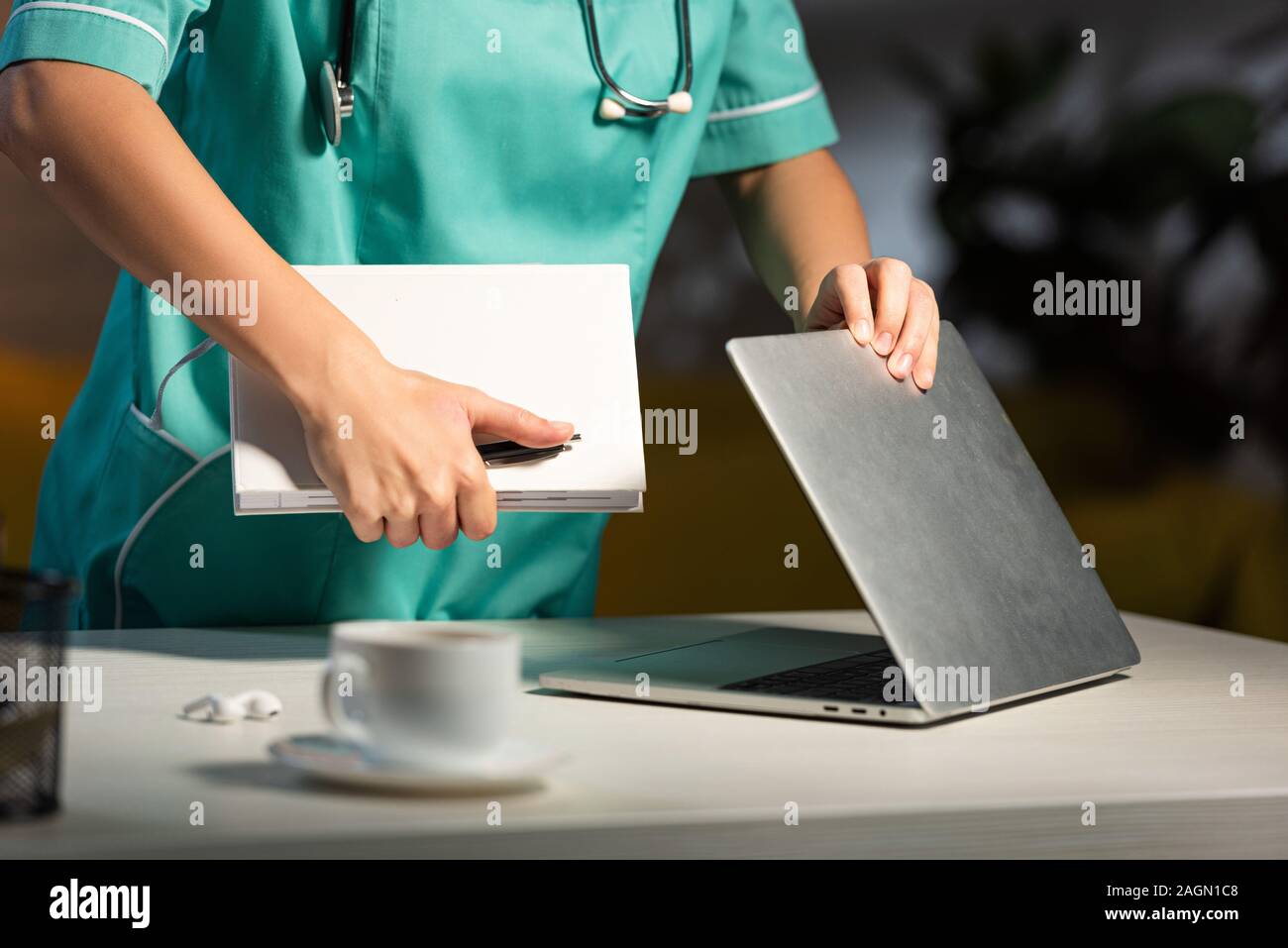 cropped view of nurse in uniform holding notebook and closing laptop ...