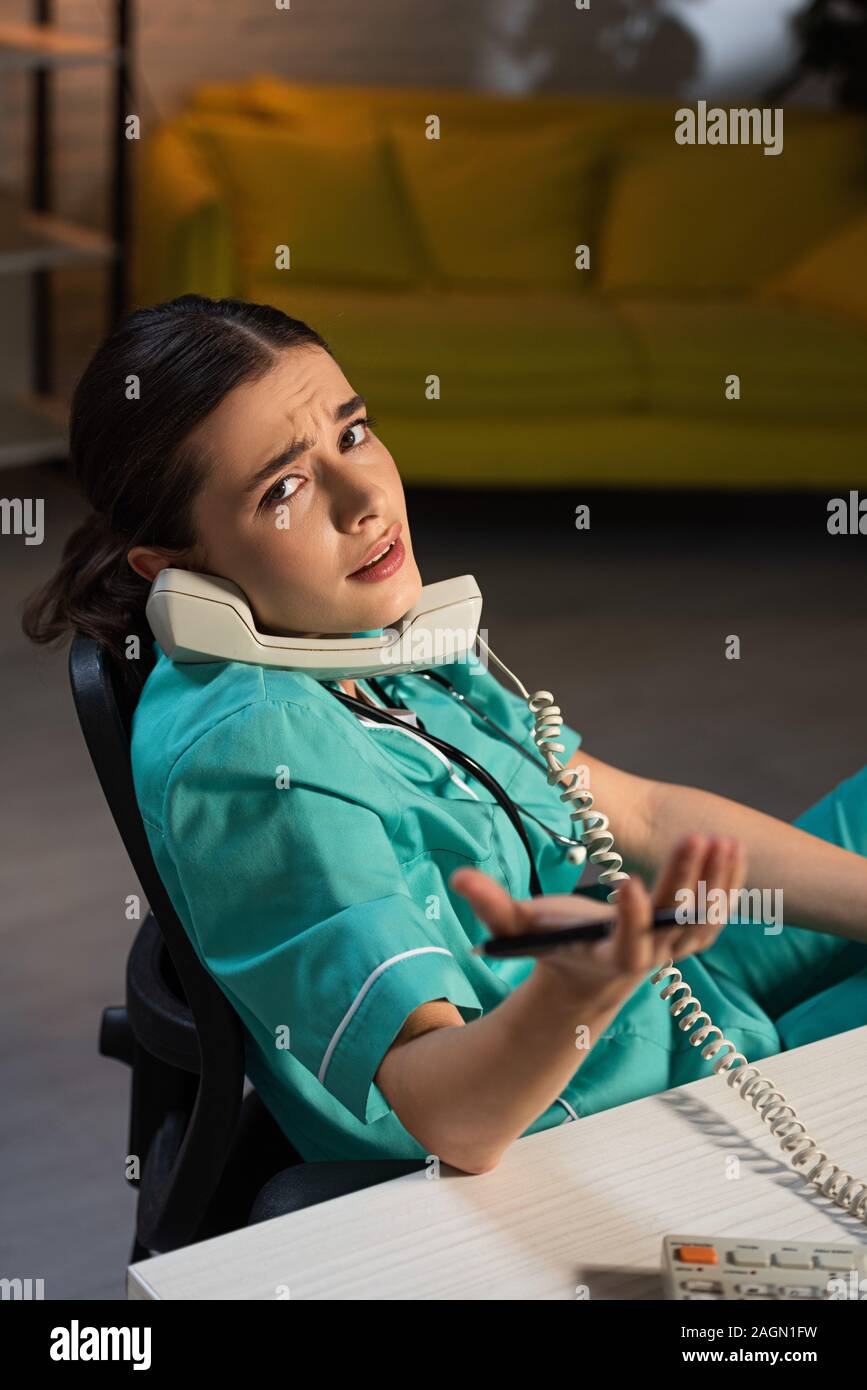 attractive nurse in uniform sitting at table and talking on telephone ...