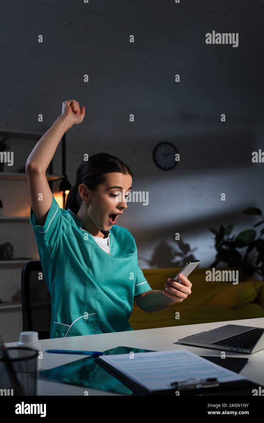 shocked nurse in uniform showing yes gesture and using smartphone ...