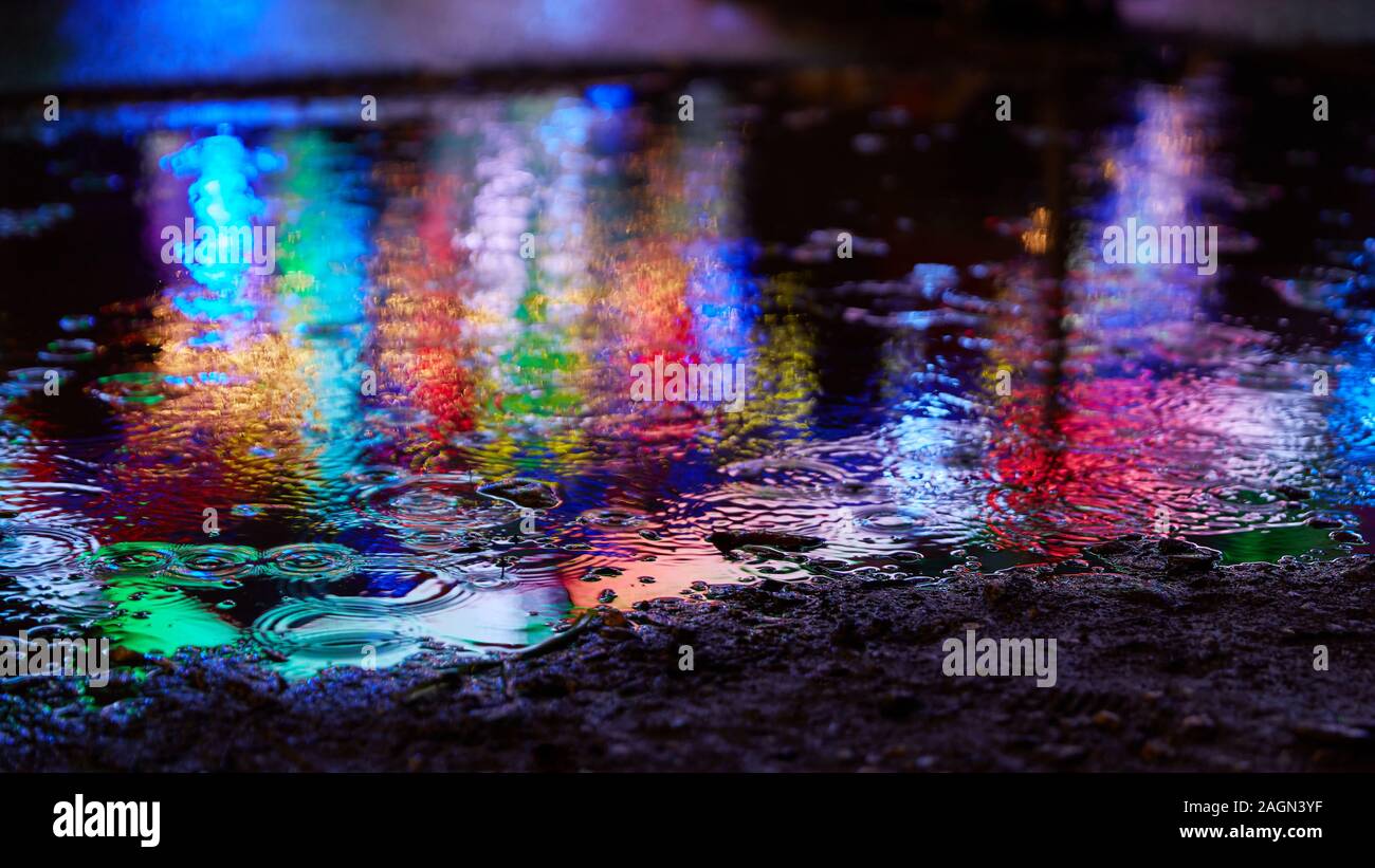 Puddle with raindrops and colored lights as a reflection in the evening ...