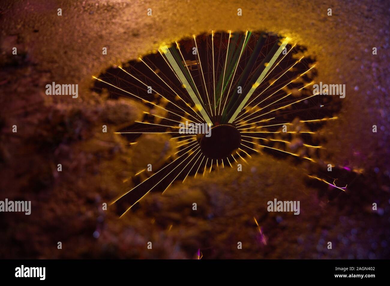 Yellow ferris wheel reflected in water from puddle at night at a fun ...