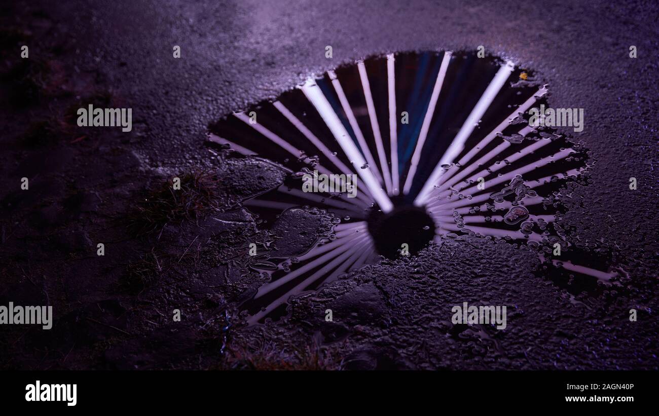 Purple neon light as a reflection in water of a puddle at a fun fair at ...