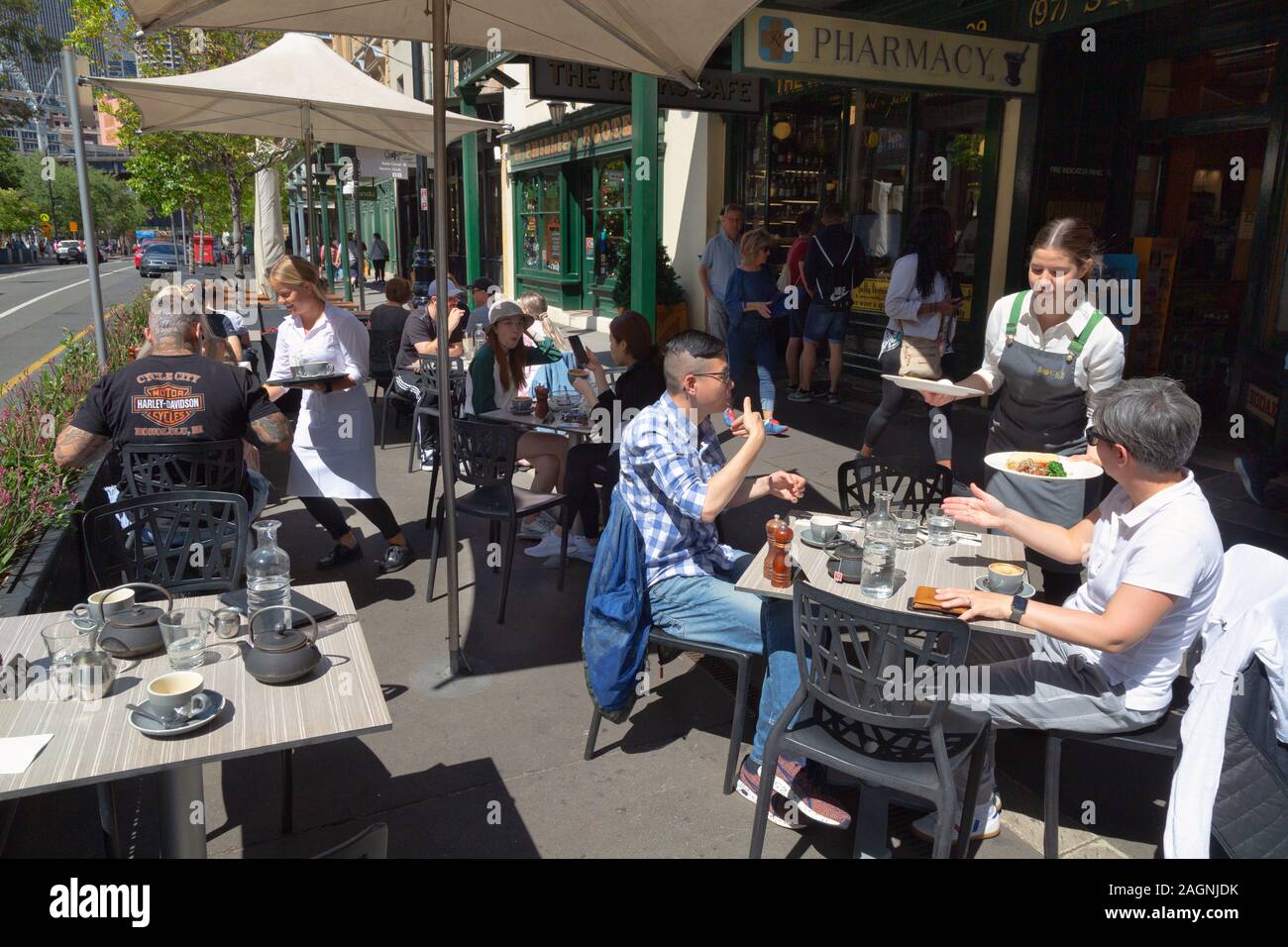 Waitress serving food to people sitting in a cafe in summer; the Rocks ...