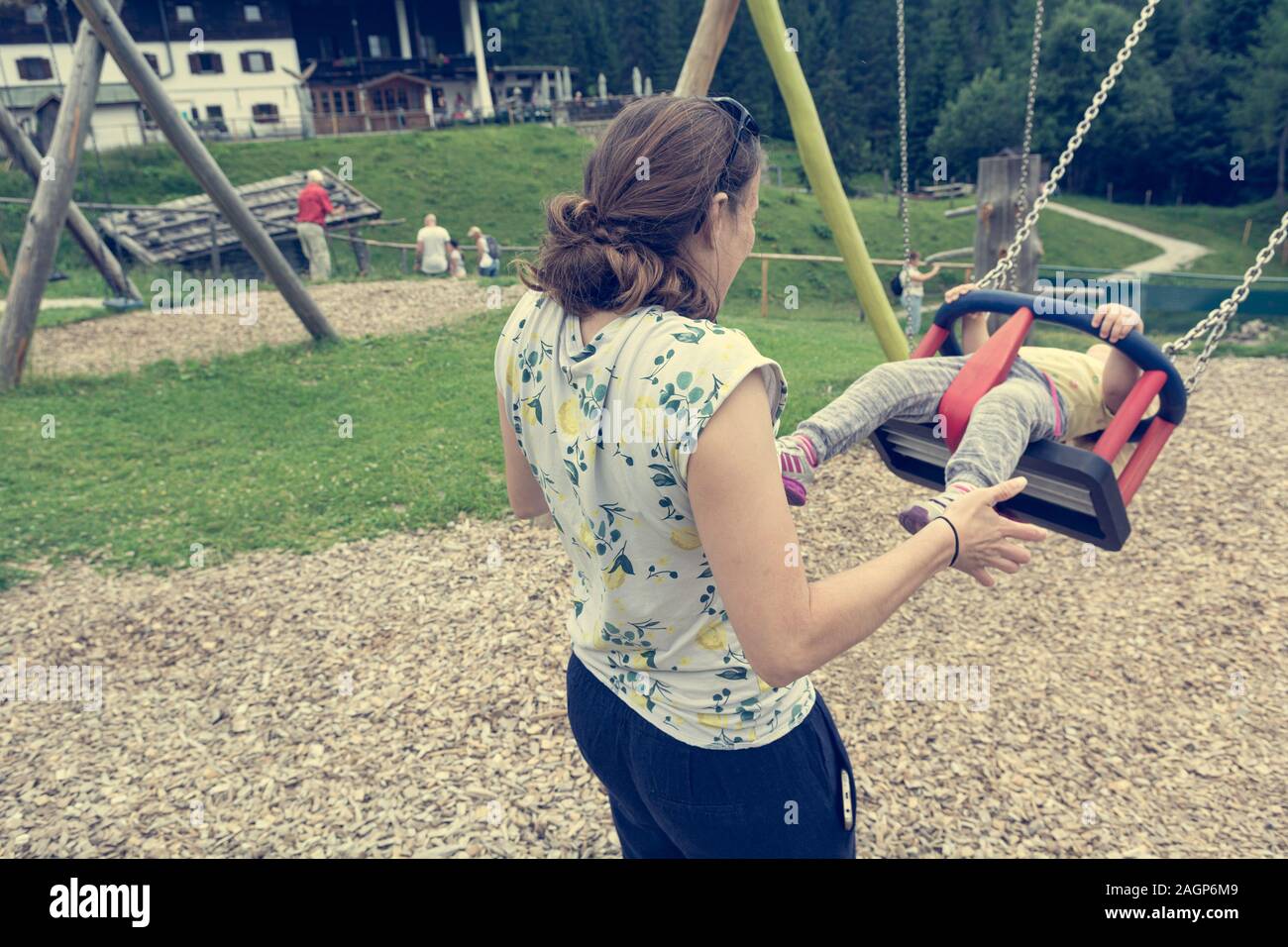 Mother pushing her daughter on a swing at outdoor playground Stock ...