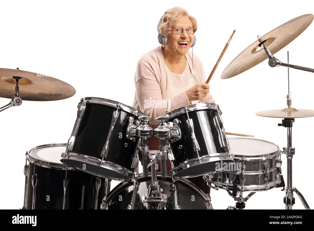 Happy elderly woman with headphones playing drums isolated on white ...