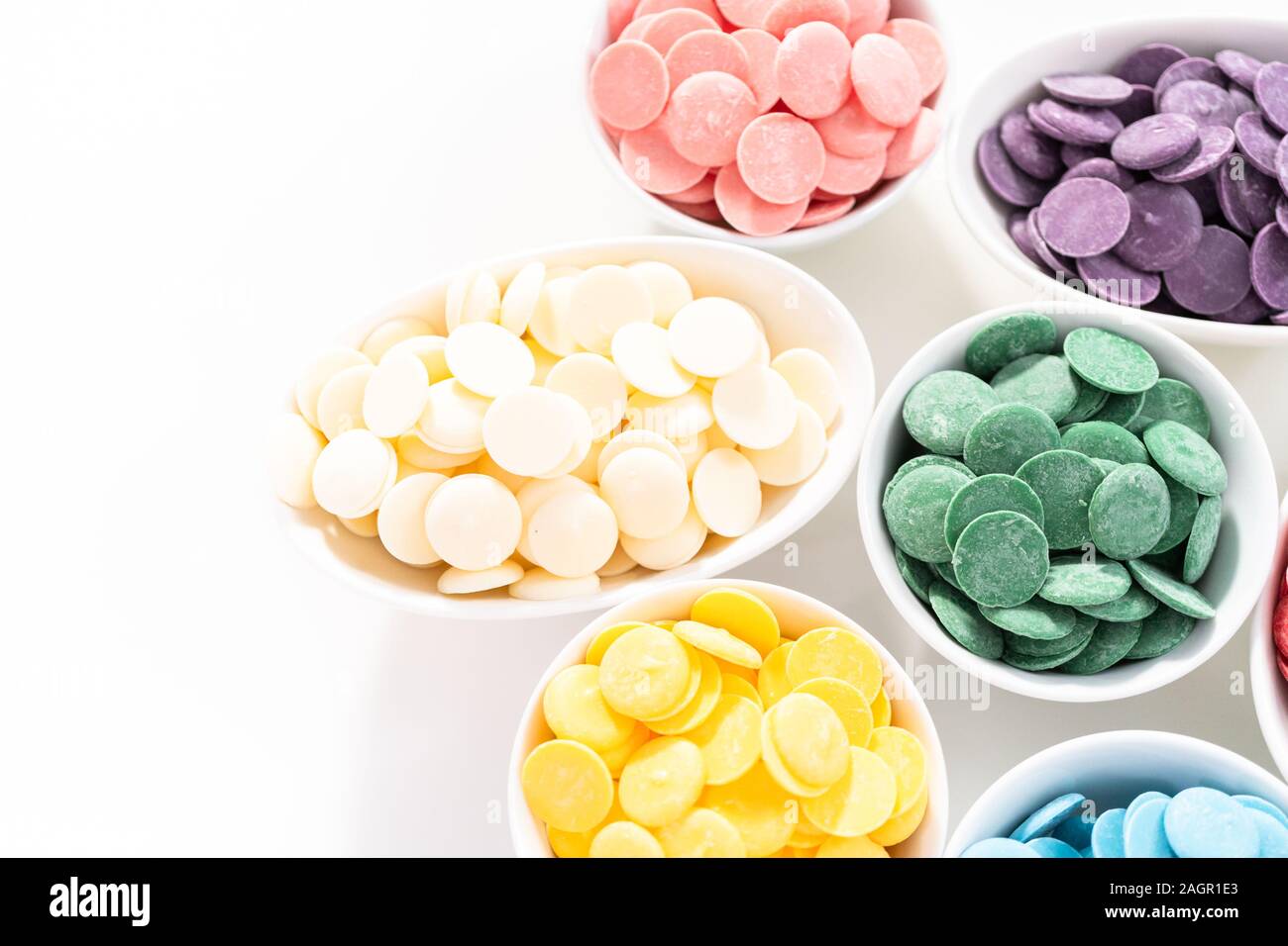 Rainbow colors of round chocolate chips in a white bowls for melting ...