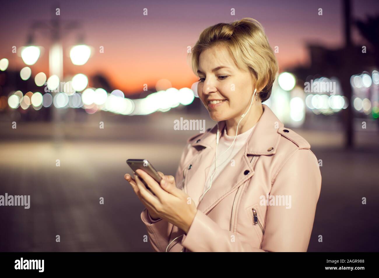 Woman using mobile phone on the street in the night time. People and ...