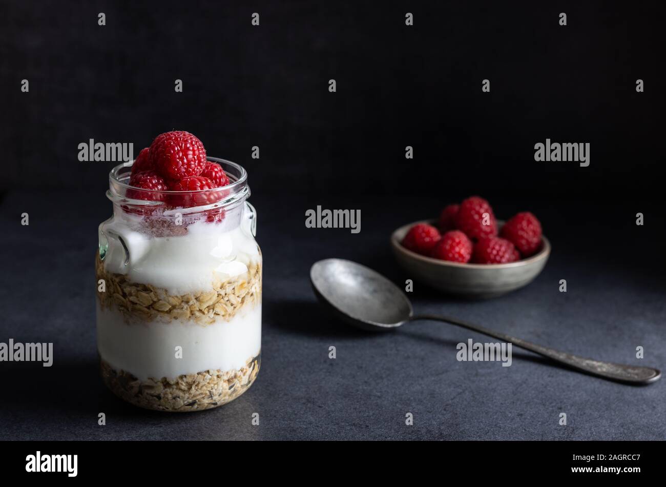 healthy vegan breakfast of yoghurt with muesli and raspberry on a dark ...