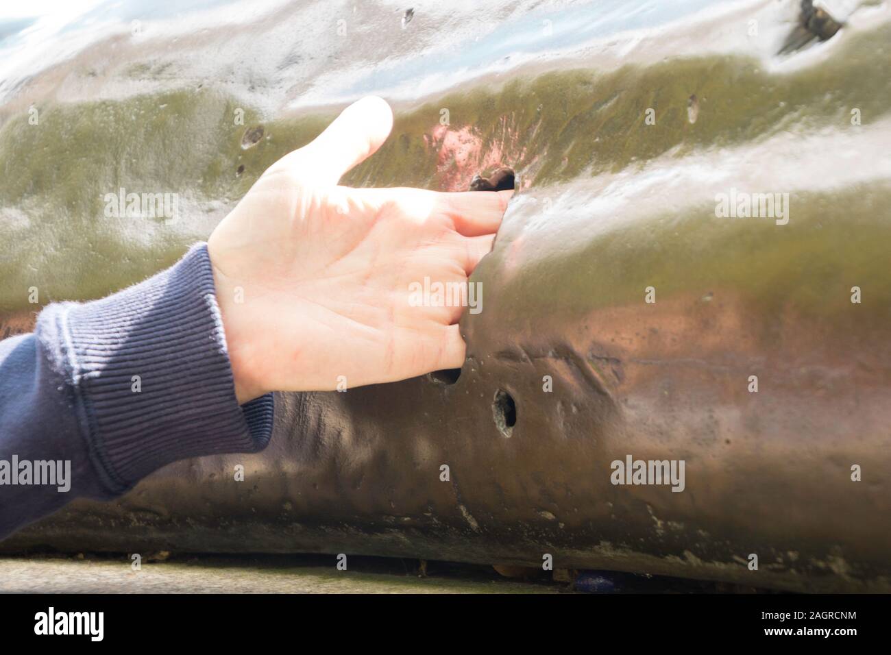 A hand inserted into a large hold in thick steel, created by a large ...