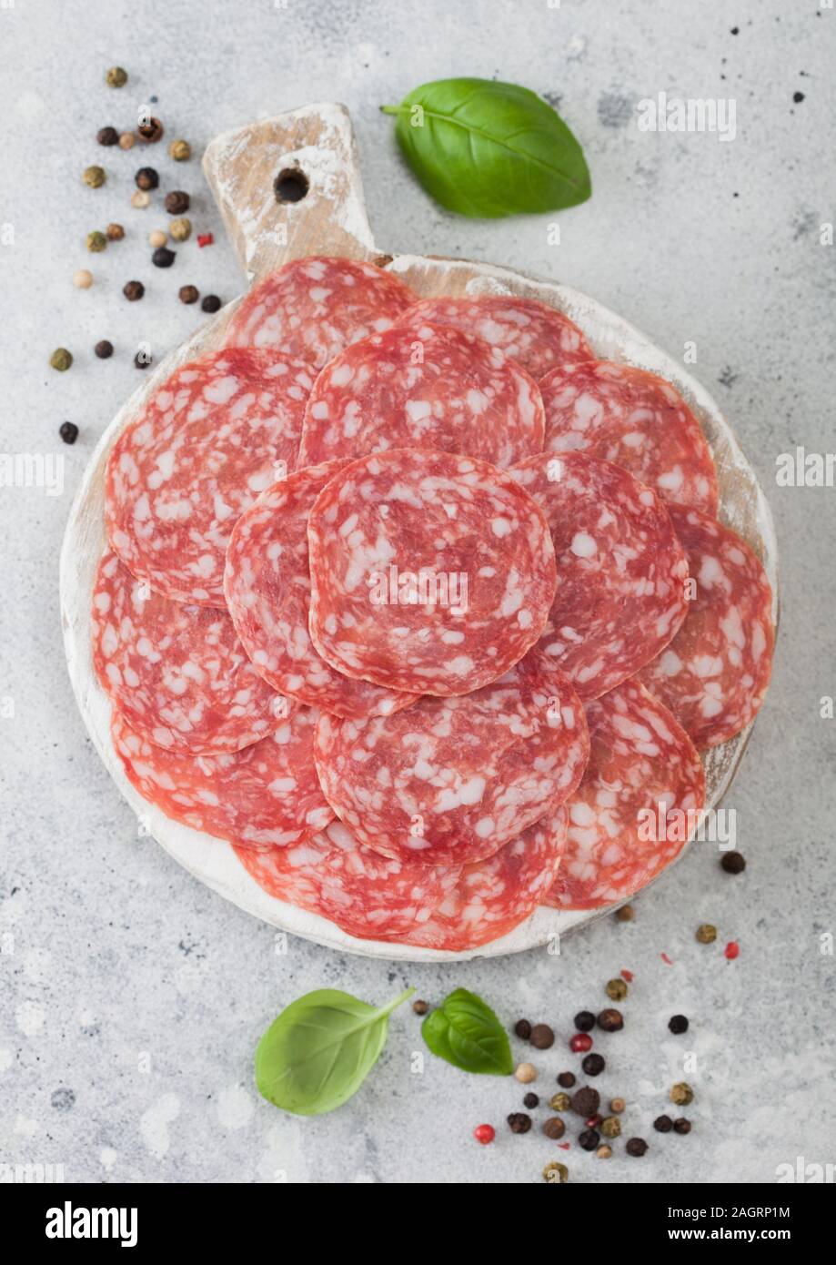 Classic salami slices with basil and pepper on round wooden chopping ...