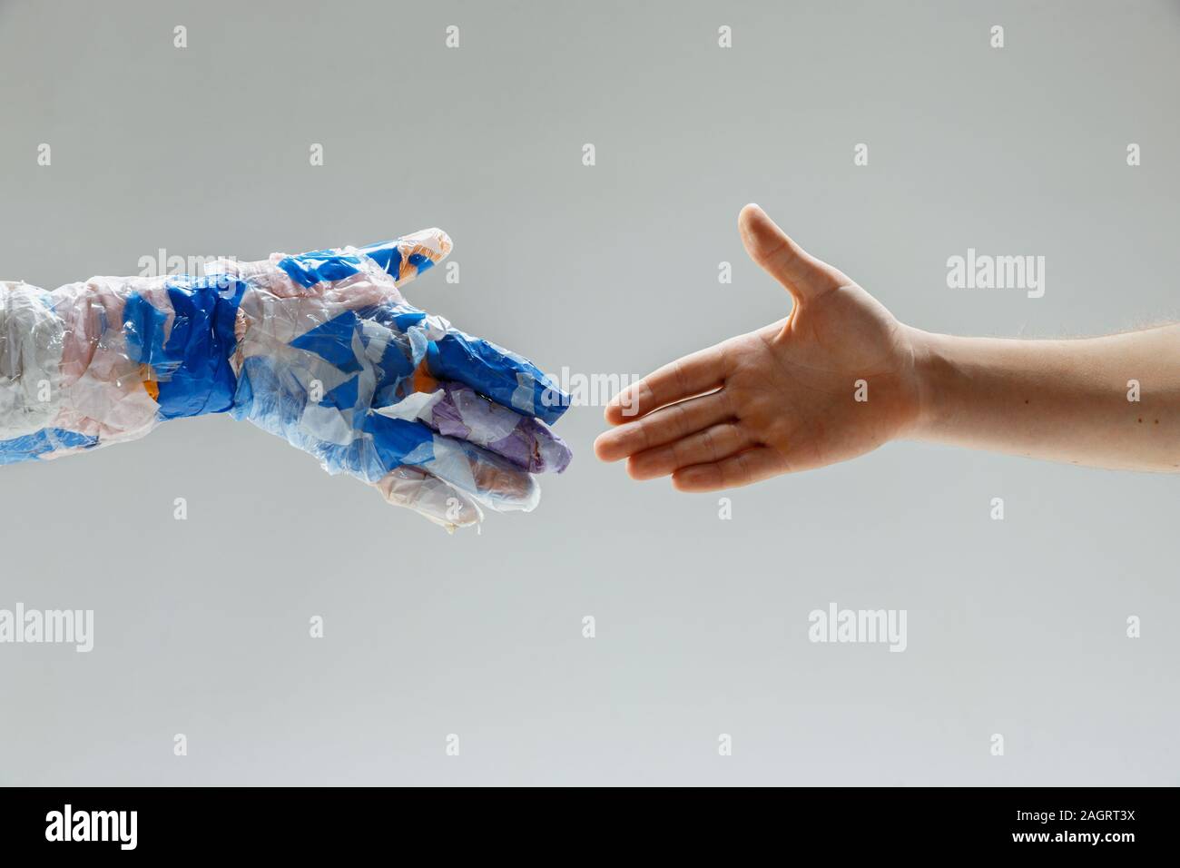 Big plastic hand made of garbage shaking another hand on white studio ...