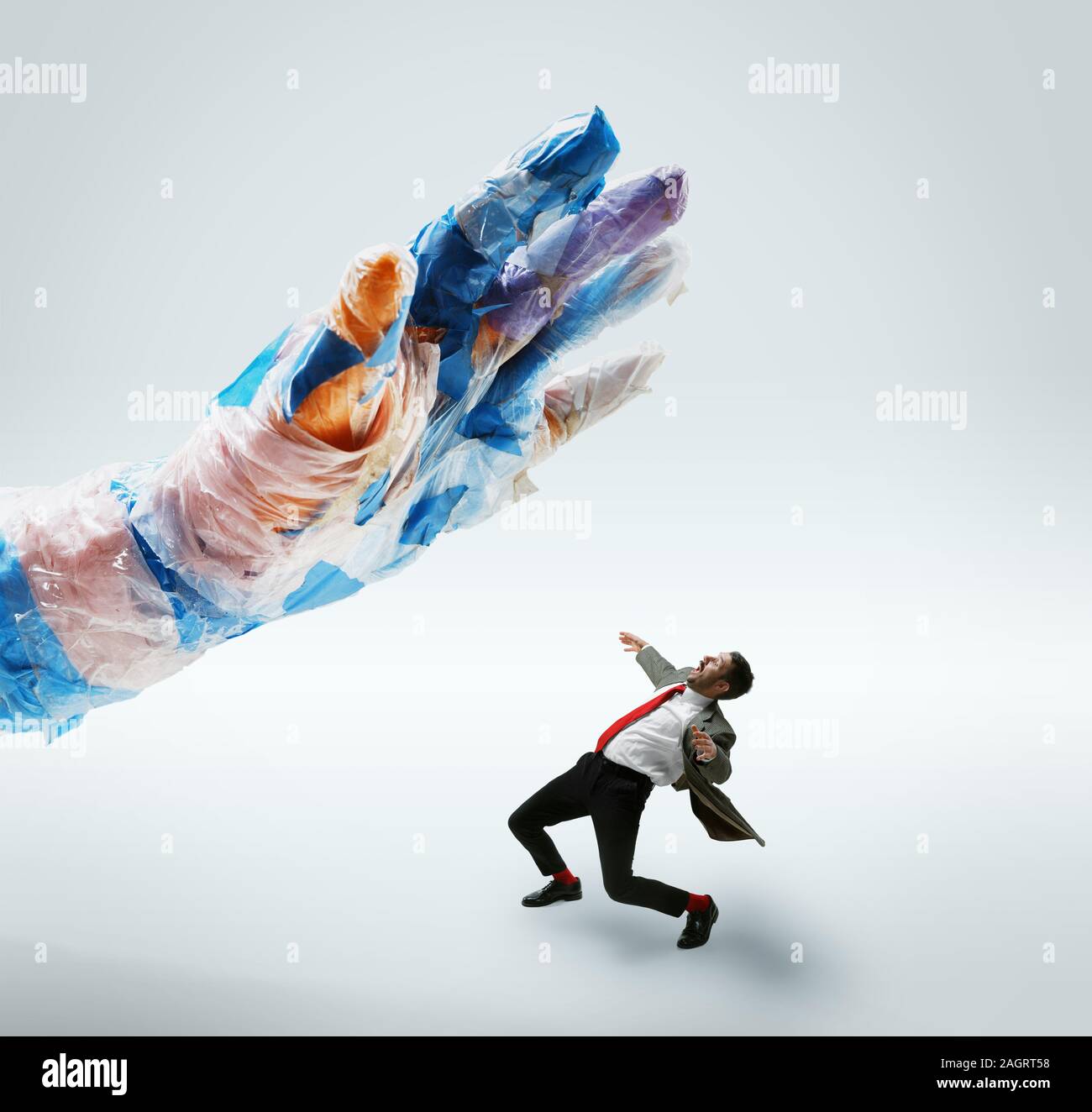Young caucasian man avoiding big plastic hand on white studio ...