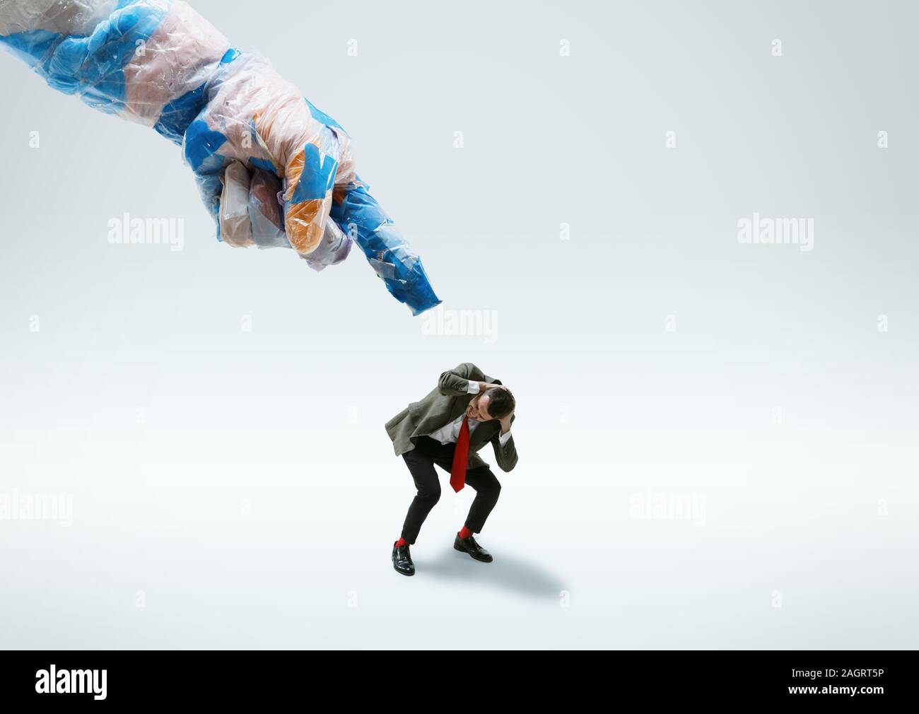 Young caucasian man avoiding big plastic hand on white studio ...