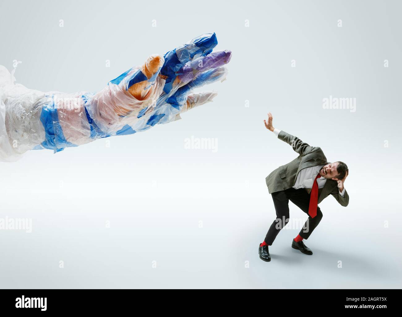 Young caucasian man avoiding big plastic hand on white studio ...