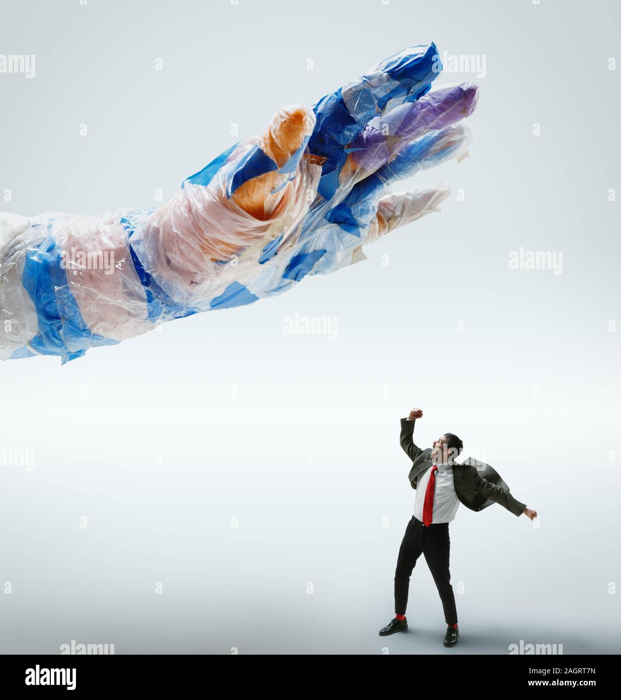 Young caucasian man avoiding big plastic hand on white studio ...