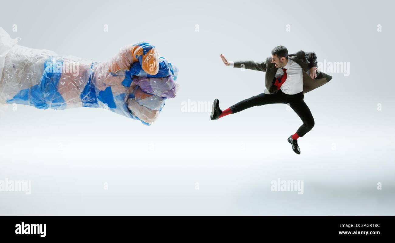 Young caucasian man avoiding big plastic hand on white studio ...
