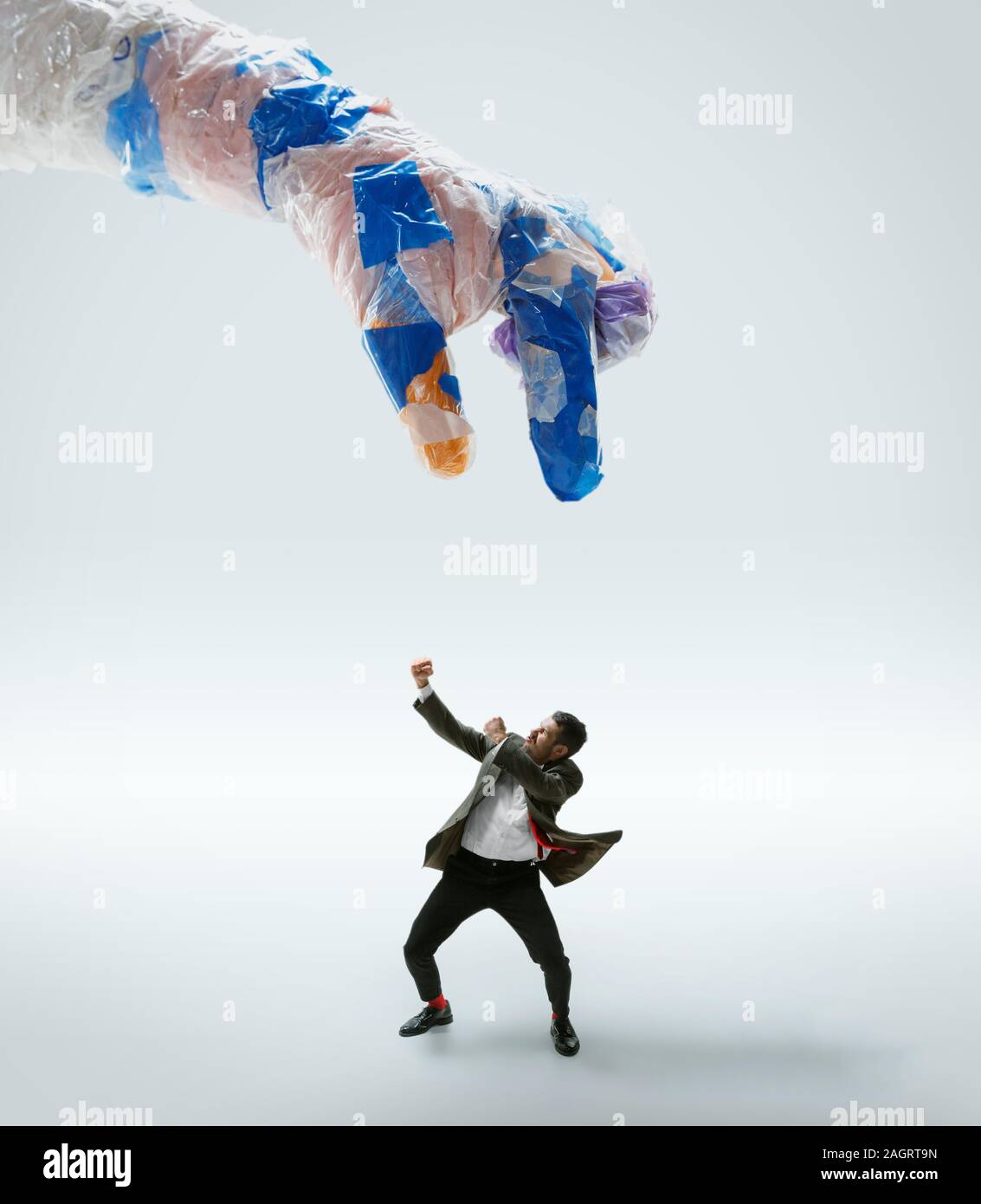 Young caucasian man avoiding big plastic hand on white studio ...