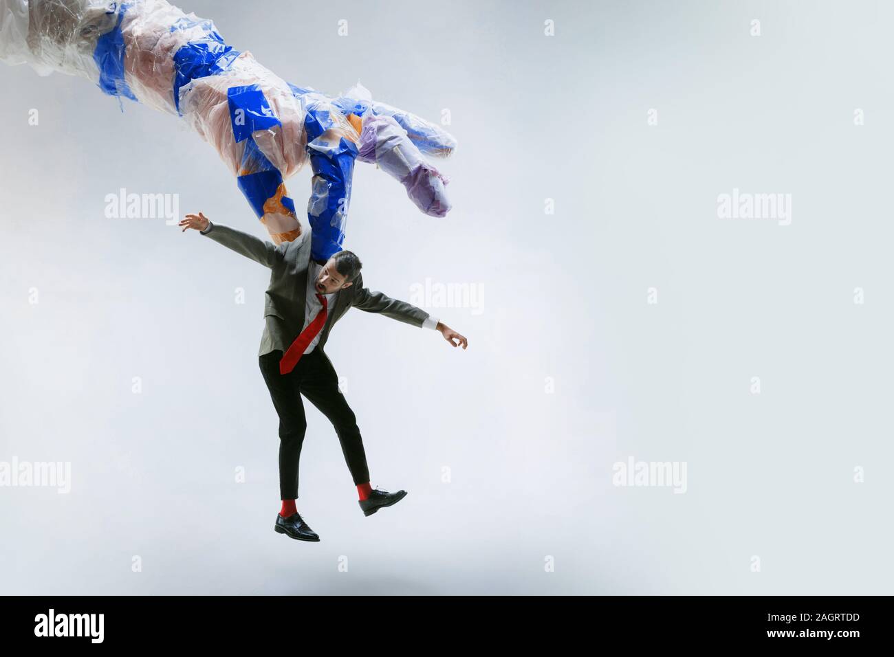Young caucasian man avoiding big plastic hand on white studio ...