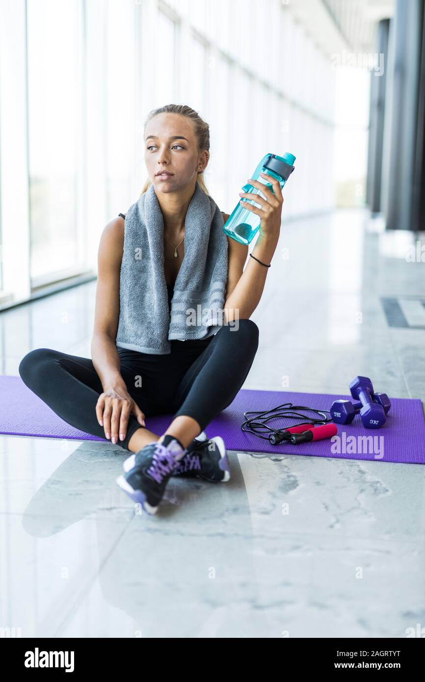 Happy fitness girl sitting relaxed on yoga mat after workout. Woman ...