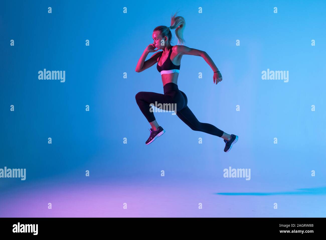 Side view of a sporty young woman jumping isolated on purple light ...