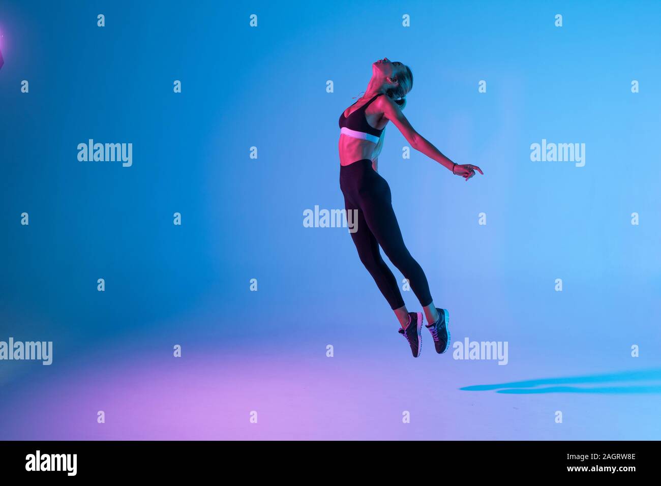 Side view of a sporty young woman jumping isolated on purple light ...