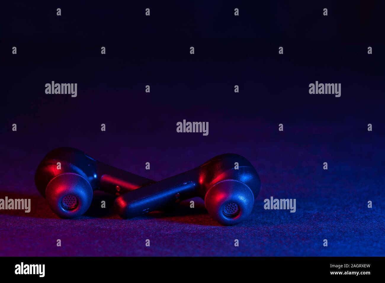 A close up photo of a pair of wireless earphone buds lit using red and ...