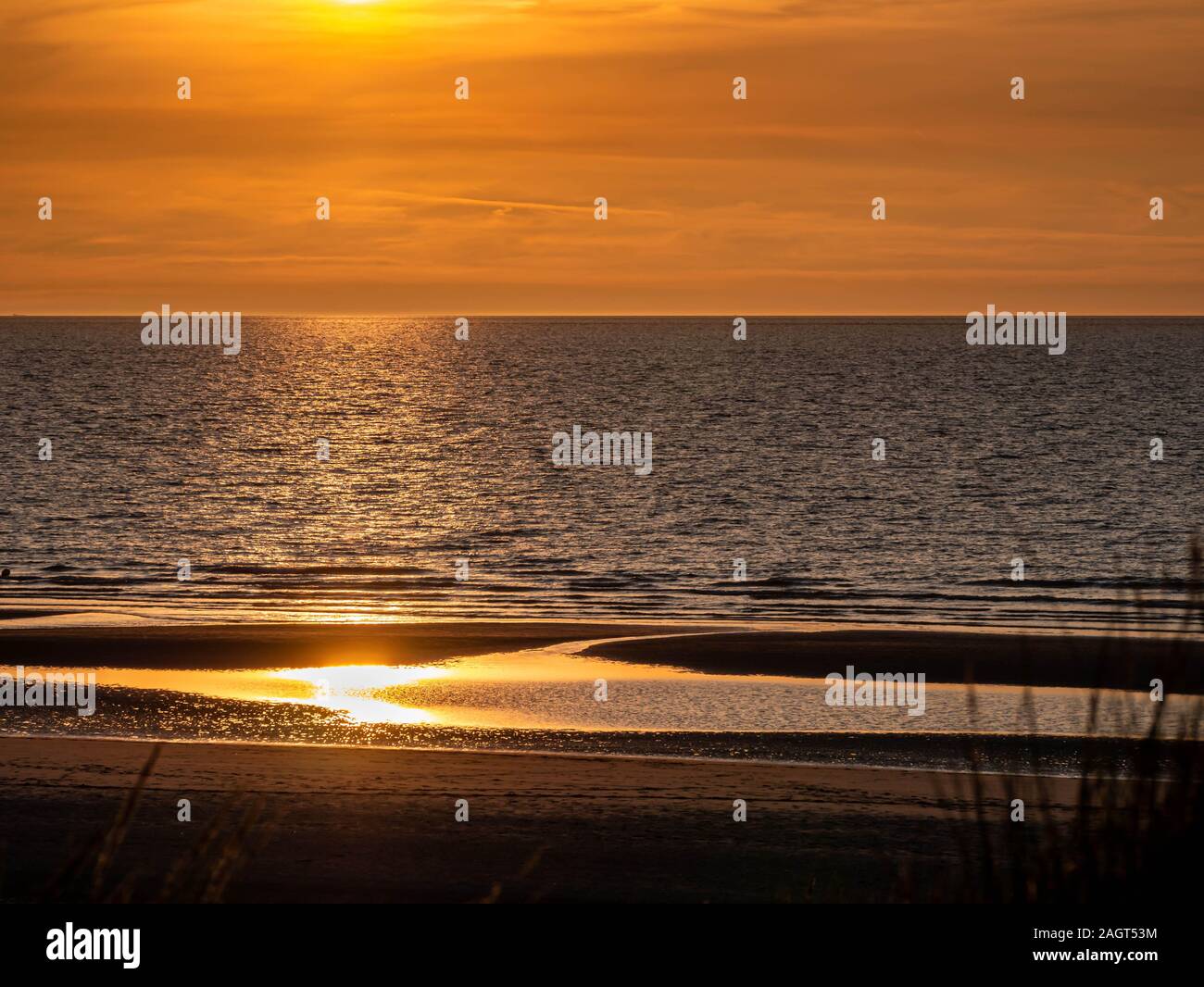 Sun setting in the ocean in front of colorful marram grass covered ...