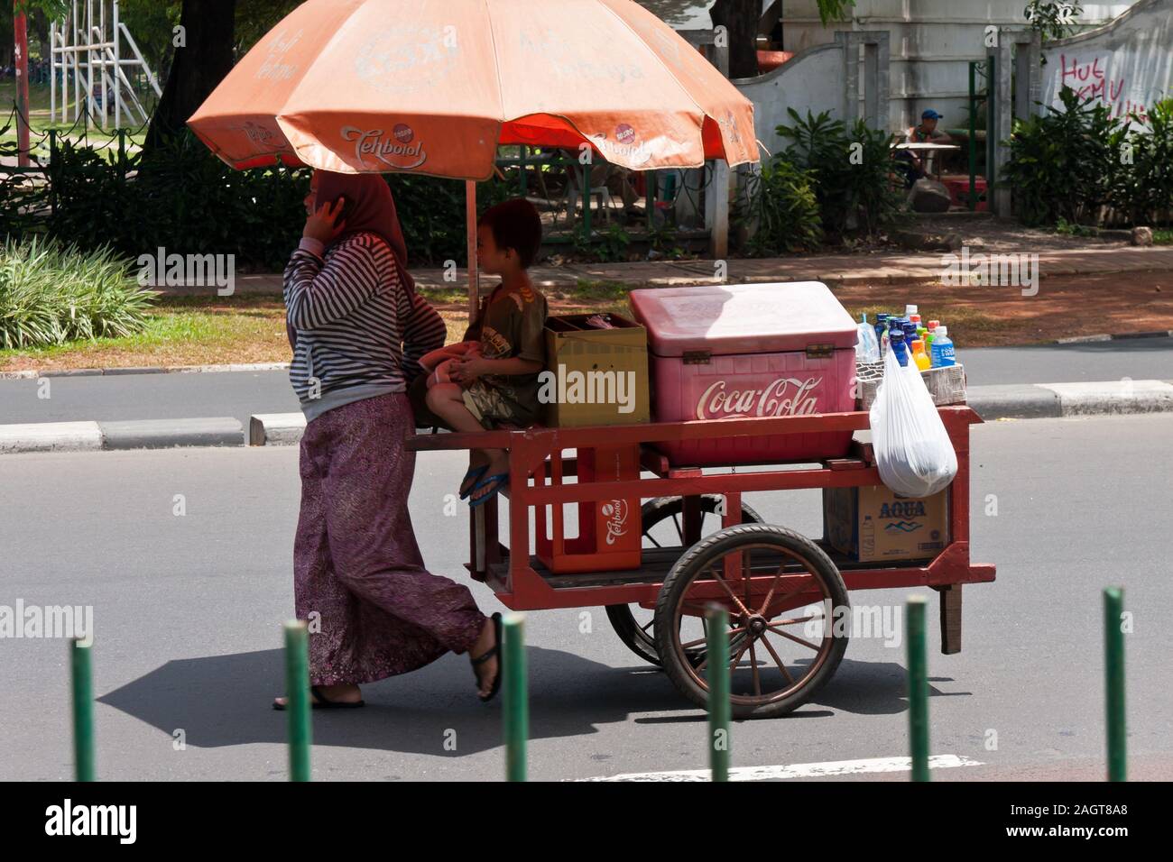 Indonesian woman with a child moving a mobile street food stall on the ...