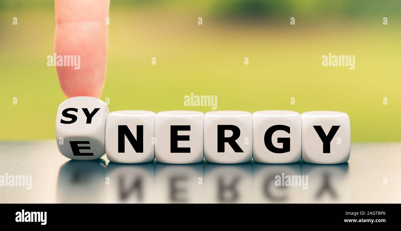 Hand turns a dice and changes the word "energy" to "synergy", or vice ...