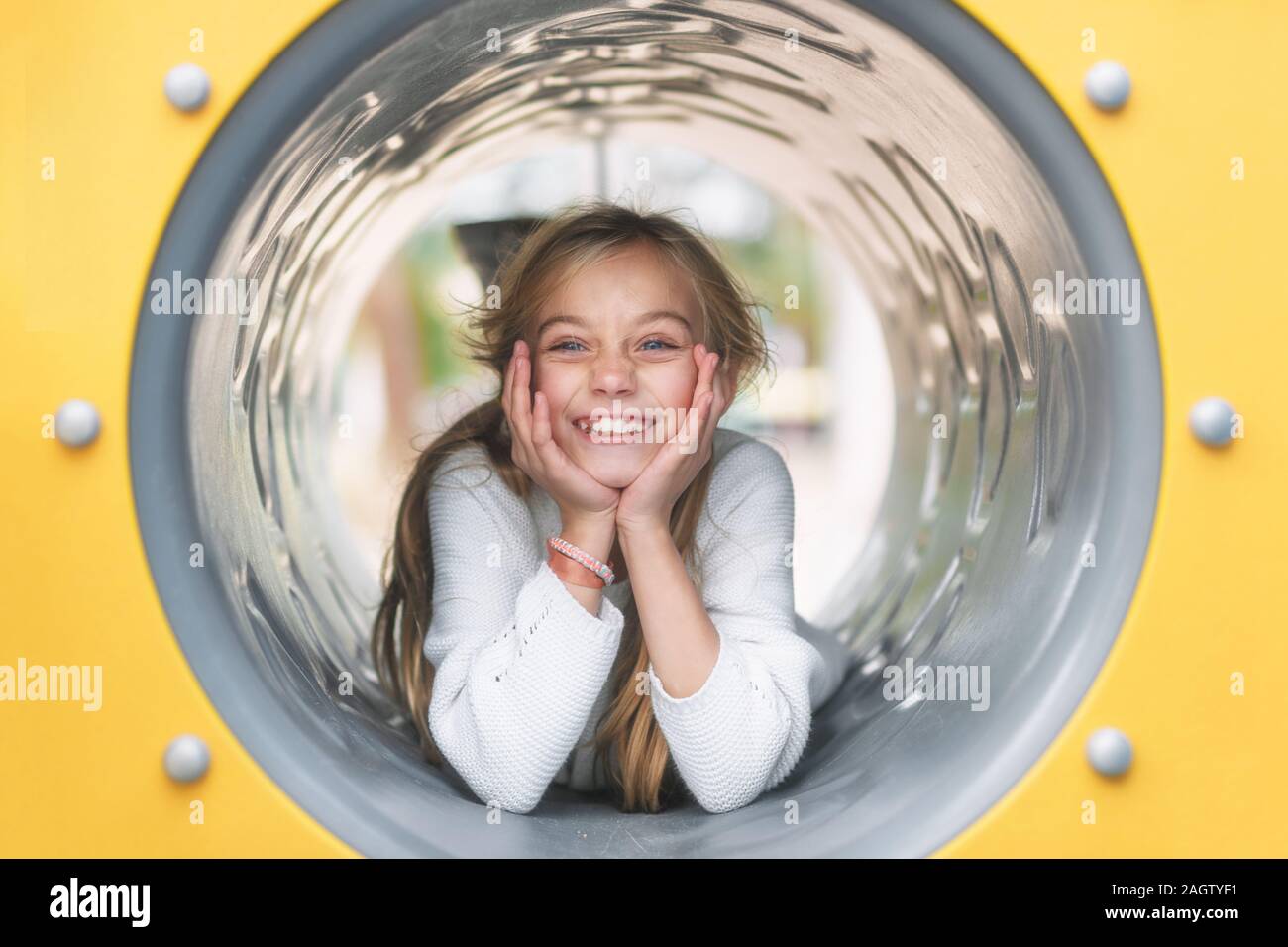 Pretty, little girl, having fun, lying on pipe on children playground ...