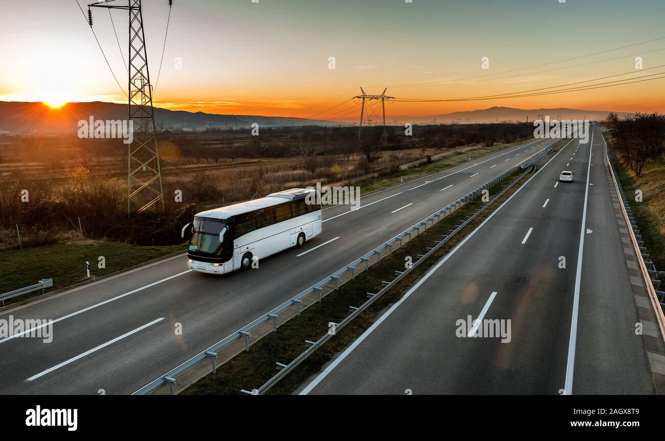 White bus traveling on a country highway under amazing orange sunset ...