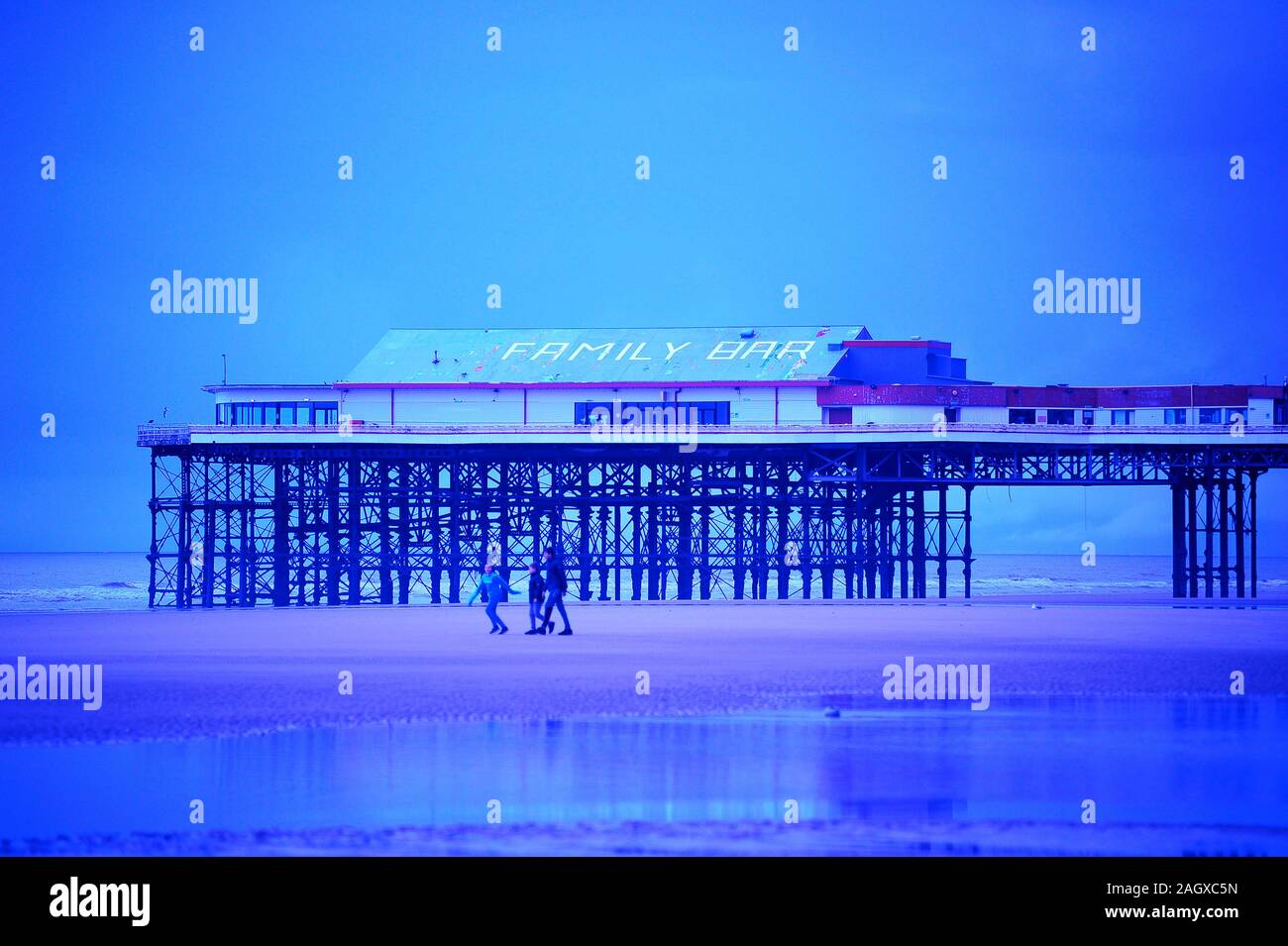 Three young people walking on Blackpool beach on a cold day in winter ...