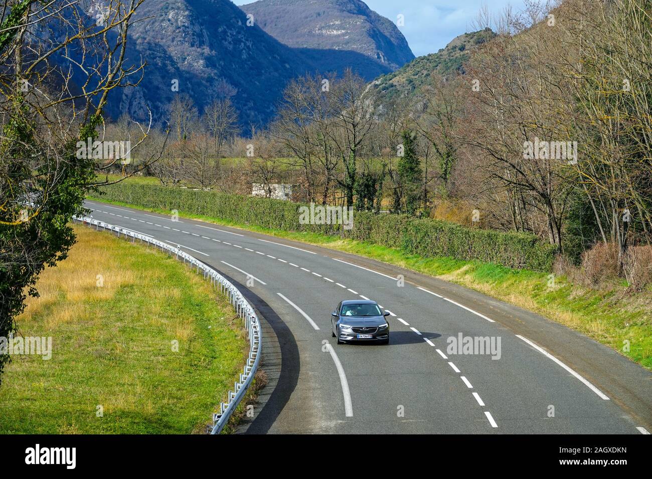 Lone silver car driving on the right on dry road with bend, France ...