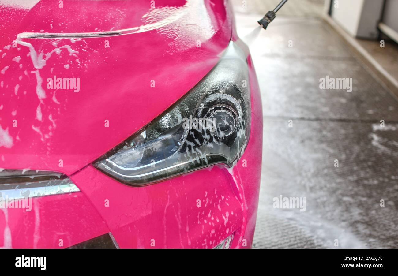 Front light of pink car washed in self serve carwash, jet water ...