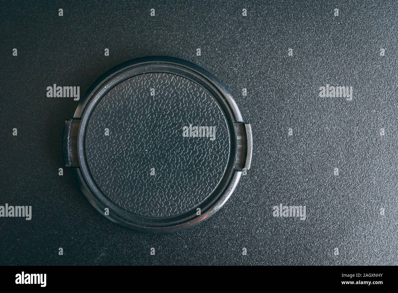 Black camera lens cap on the black textured table. Flat lay with copy ...
